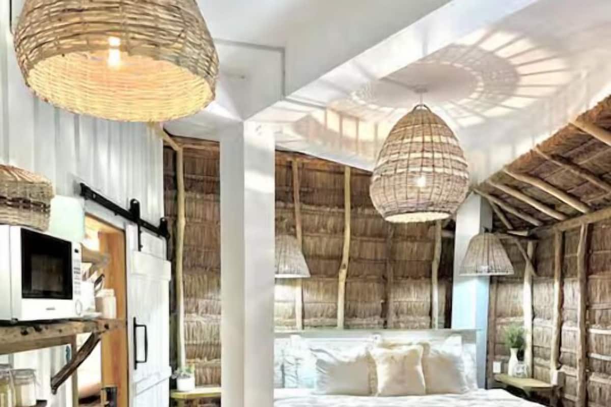 Quarto com uma cama grande, uma escrivaninha de madeira, uma pia branca e luminárias de teto em tear.