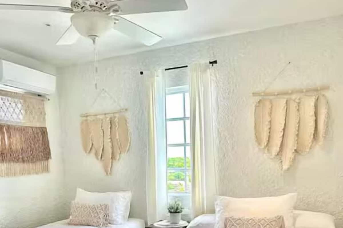 Quarto com duas camas, um ventilador de teto e uma janela com cortinas.