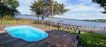Piscina em um deck de madeira com vista para um lago e um barco ao longe.