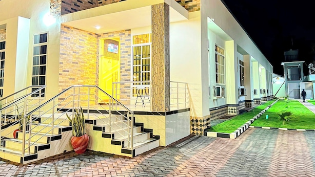 Um edifício moderno com uma escadaria que leva a uma entrada luminosa, uma antena parabólica no telhado e um gramado bem cuidado.