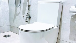 Um banheiro moderno com vaso sanitário branco, chuveiro e piso ladrilhado.