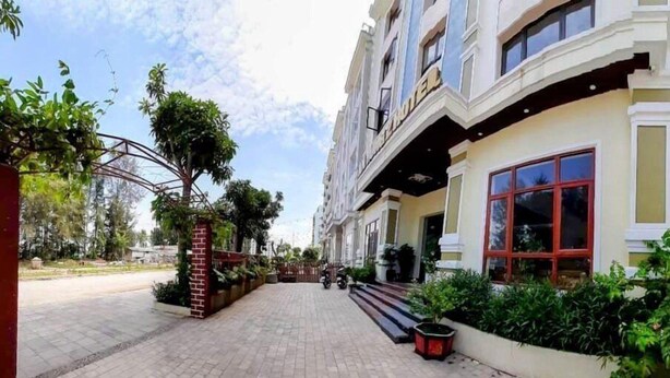 Entrada de hotel com caminho de paralelepípedos, um pilar de tijolos e uma área coberta com degraus que levam à entrada.