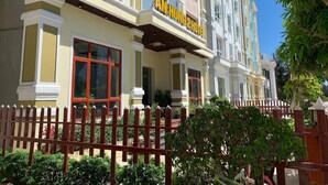 Um hotel de vários andares com fachada amarela, janelas emolduradas em vermelho e uma placa com o nome visível.