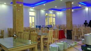 Uma ampla sala de jantar com várias mesas e cadeiras, um grande buffet montado, e um design moderno no teto com detalhes de iluminação azul.