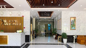 Uma área de recepção de hotel com design moderno, apresentando um balcão de atendimento, um painel de parede de madeira com o nome do hotel e um piso de mármore.