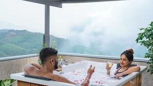 Um casal em uma banheira de hidromassagem com vista panorâmica de colinas e névoa.