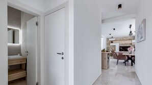 Cozinha moderna com painel de backsplash de pedra, área de jantar com mesa e cadeiras, e corredor que leva a um banheiro com espelho e pia.