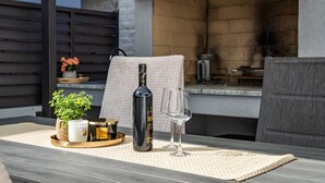 Uma mesa com uma garrafa de vinho, um copo, uma bandeja com uma planta e velas, e um muro de tijolos ao fundo.
