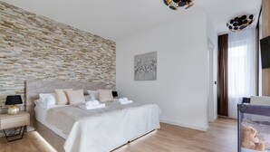 Quarto moderno com uma cama grande, uma mesa de cabeceira com luminária, uma obra de arte na parede e piso de madeira.