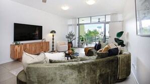 Uma sala de estar moderna com uma televisão de tela plana grande, um armário de madeira, um sofá verde e um espaço de jantar com mesa e cadeiras.