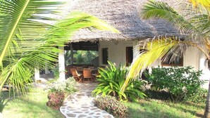 Uma casa com telhado de palha e um caminho pavimentado que leva a uma mesa e cadeiras de madeira.