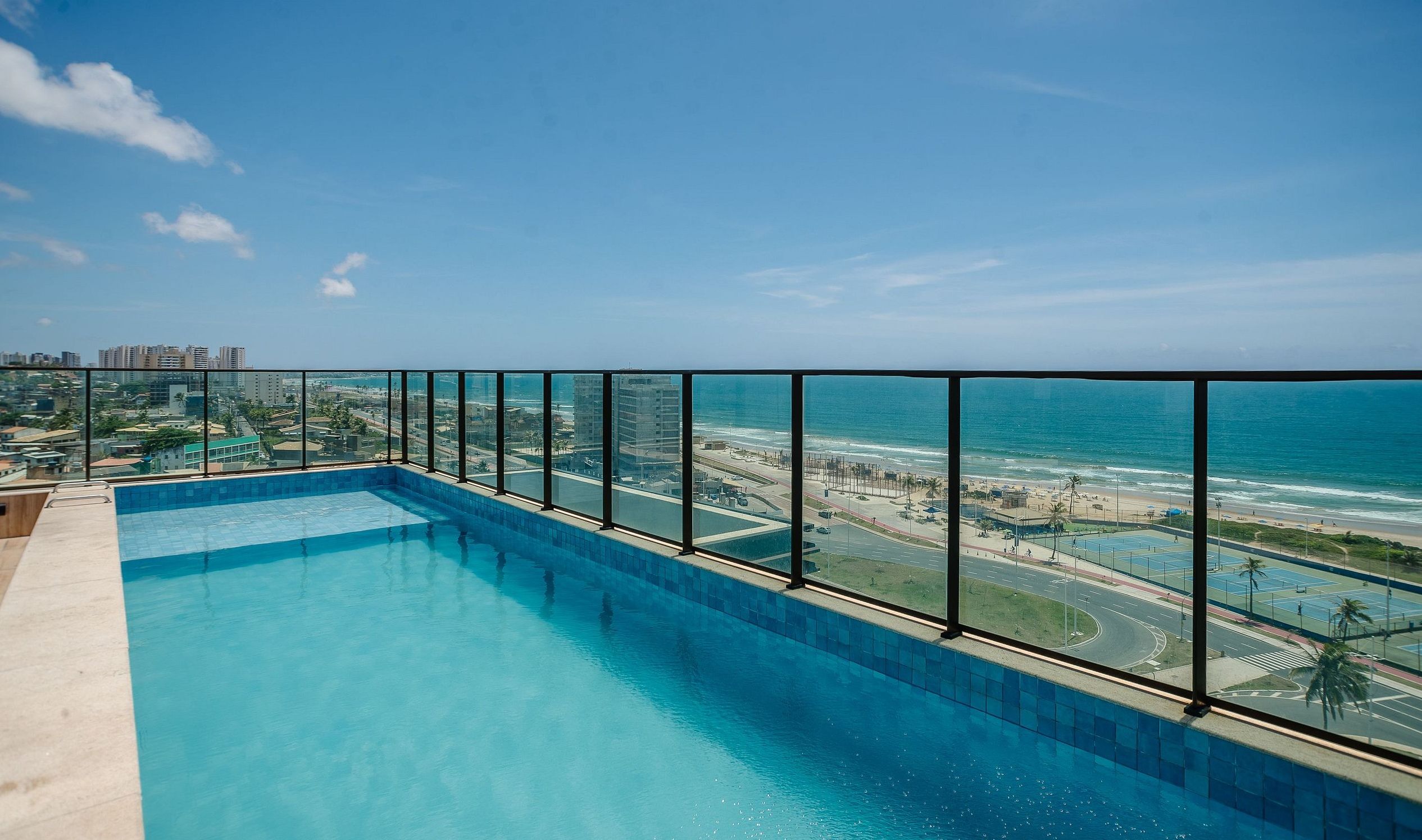 Piscina no terraço com vista para a praia e o horizonte urbano.