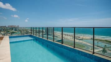 Piscina no terraço com vista para a praia e o horizonte urbano.