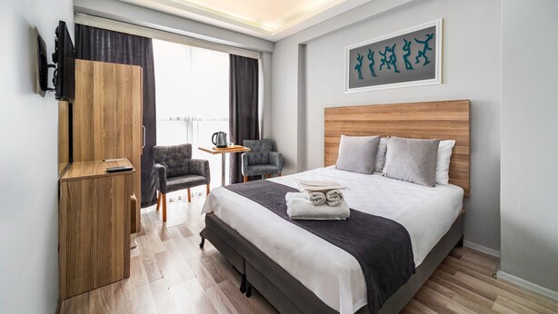 Quarto de hotel moderno com uma cama grande, guarda-roupa de madeira, secretária, cadeira e televisão.