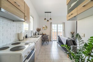 Cozinha moderna com eletrodomésticos brancos, armários de madeira e um espaço de refeições com sofá e mesa cinzas.