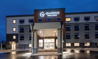 Edifício do GrandStay Hotel & Suites com design moderno, apresentando uma entrada notável com portas de vidro e uma cobertura.