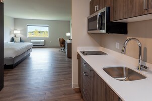 Um apartamento moderno com cozinha, equipado com pia de aço inoxidável, micro-ondas e armários de madeira. Uma grande janela oferece vista para o exterior.