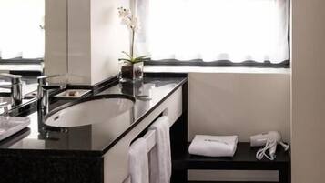 Casa de banho moderna com lavatório de bancada preta, espelho, toalha branca e pequena prateleira com toalha e secador de cabelo.
