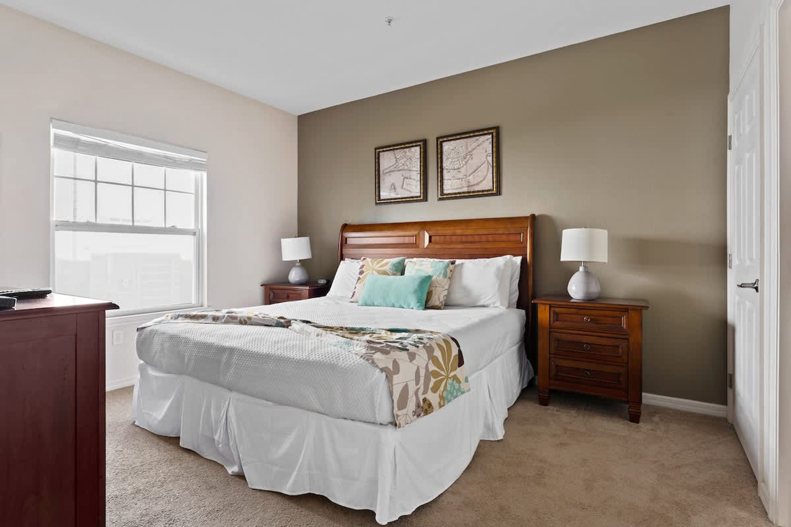 Quarto com uma cama grande, duas mesas de cabeceira com luminárias, cômoda e janela.