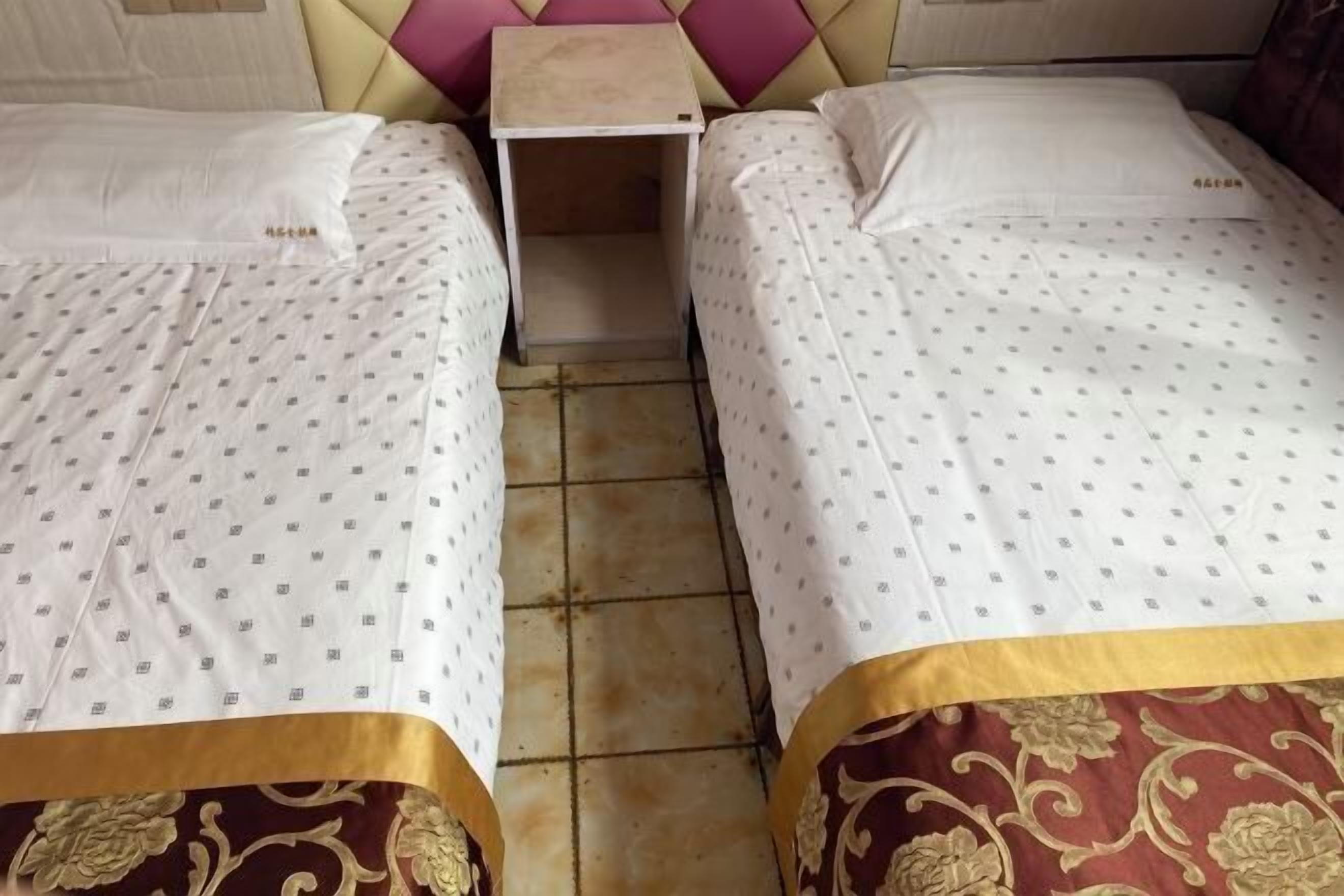 Quarto de hotel com duas camas de solteiro, uma mesinha de cabeceira e cabeceira com padrão de losangos.