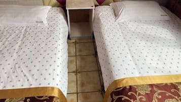 Quarto de hotel com duas camas de solteiro, uma mesinha de cabeceira e cabeceira com padrão de losangos.