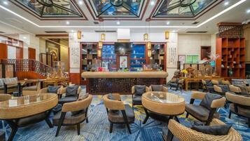 Um hall de hotel com mobiliário de vime, área de bar e teto com detalhes elaborados.