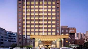 Um hotel com vários andares, entrada destacada e estacionamento cheio de carros.