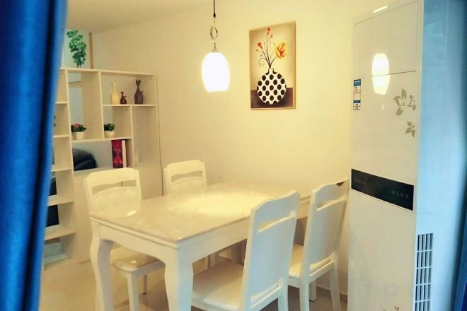 Uma sala de jantar com mesa e cadeiras brancas, geladeira e luminária fixada na parede.