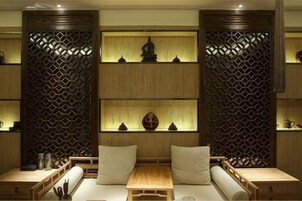 Quarto tradicional com divisória de madeira, estantes com objetos decorativos, área de estar acolchoada e uma pequena mesa.