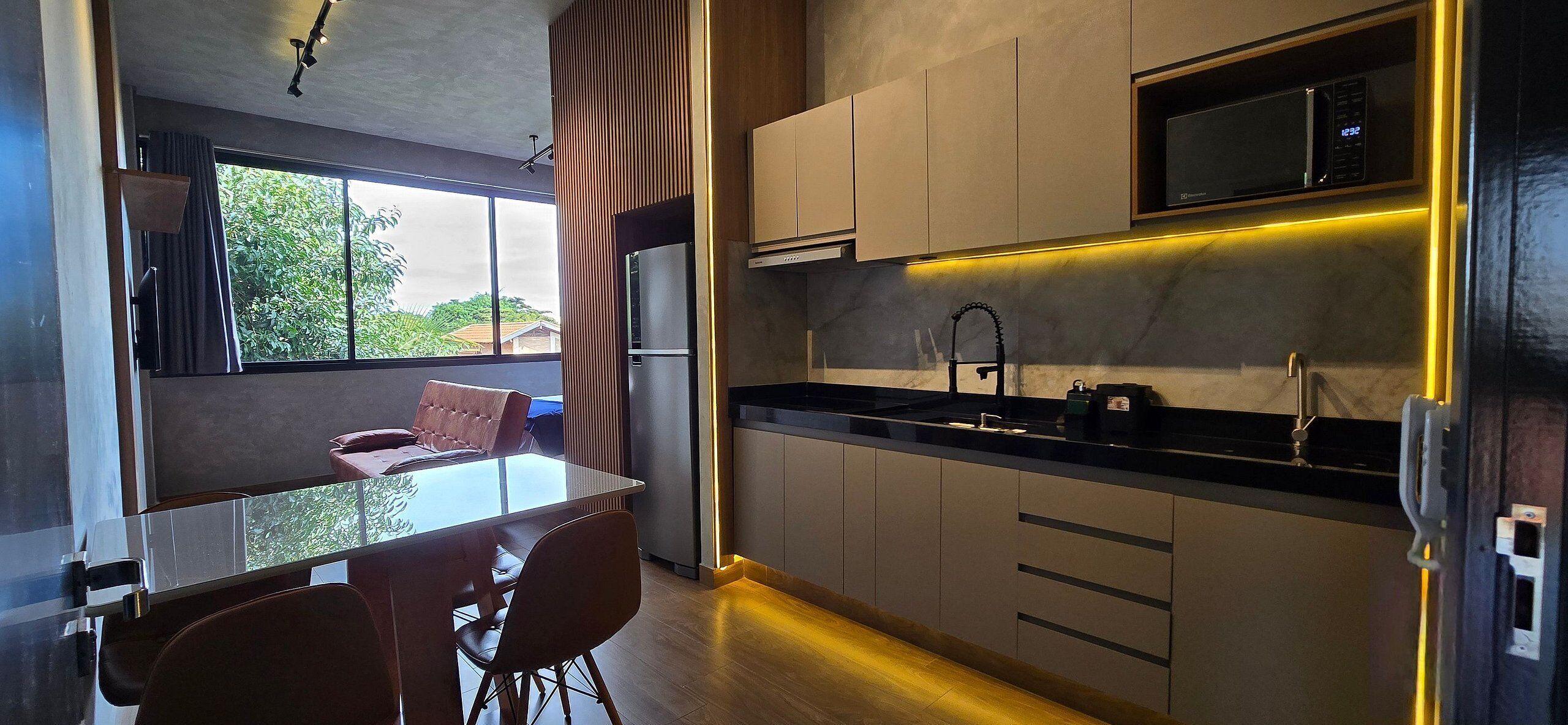 Cozinha moderna com micro-ondas embutido, pia e área de refeições com mesa e cadeiras.