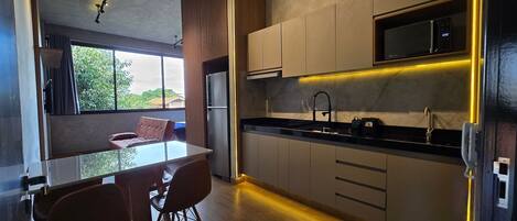 Cozinha moderna com micro-ondas embutido, pia e área de refeições com mesa e cadeiras.
