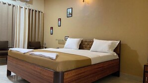 Quarto de hotel com cama grande, cabeceira de madeira, mesa de cabeceira, cadeira e cortina.