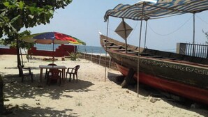 Uma praia com um barco tradicional, uma mesa com cadeiras e um guarda-sol colorido.