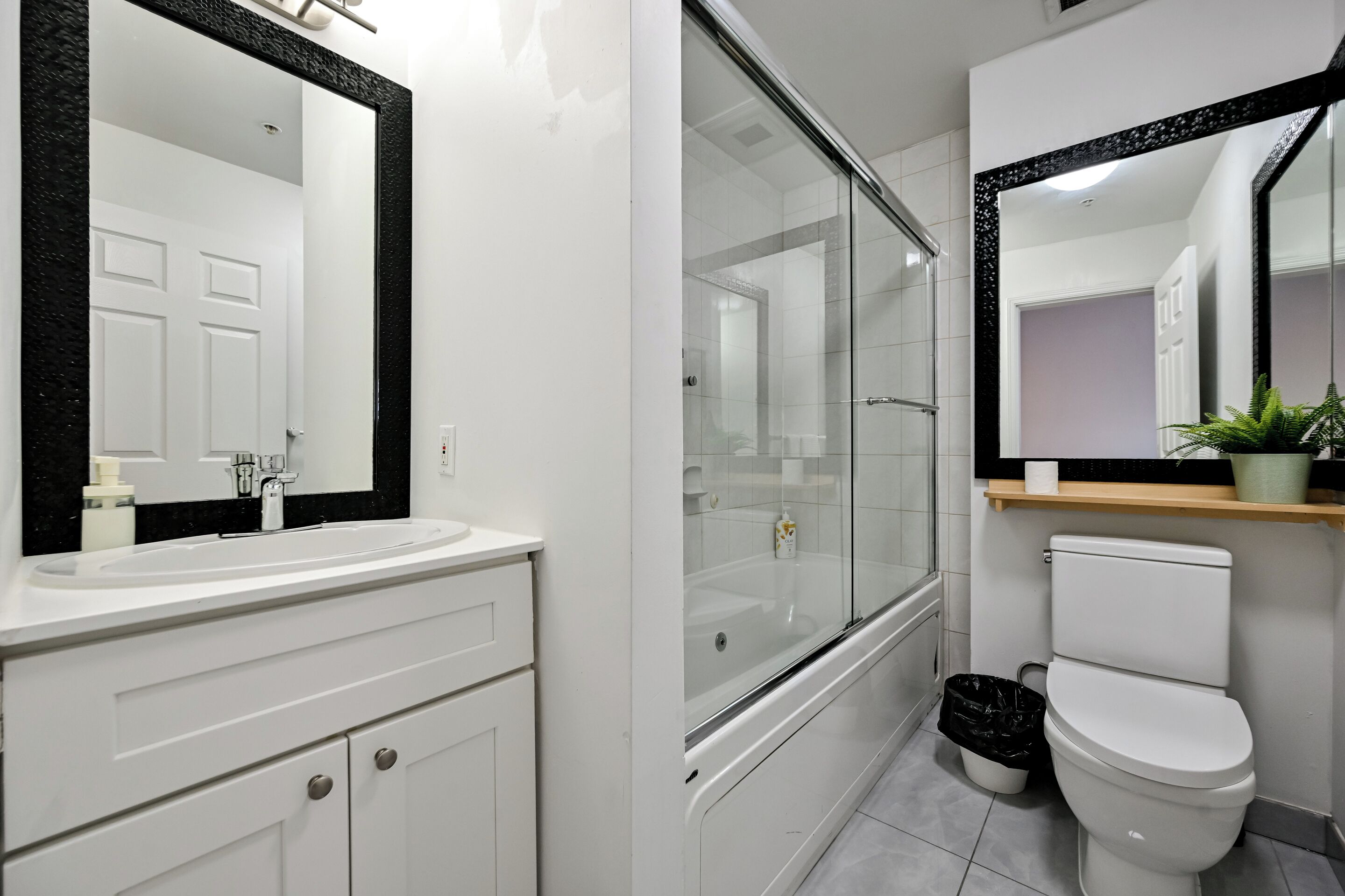 Uma casa de banho moderna com uma sanita, um lavatório branco, um espelho grande e uma cabine de duche com vidro.