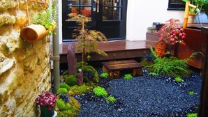 Um jardim com muro de pedra, um banco de madeira e diversas plantas.