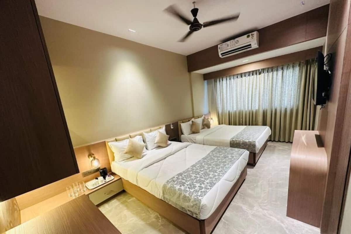 Quarto de hotel com duas camas, ventoinha no teto, aparelho de ar condicionado, televisão e escrivaninha de madeira com luminária.