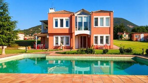 Uma casa de dois andares com piscina, um pátio com mobiliário de exterior e um cenário montanhoso.
