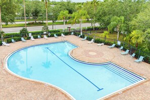 Uma piscina com deck ladrilhado, rodeada por espreguiçadeiras e palmeiras.