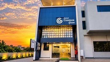 Um hotel moderno com um letreiro grande e chamativo 'Hotel Cosmos Green', janelas amplas e entrada bem iluminada.