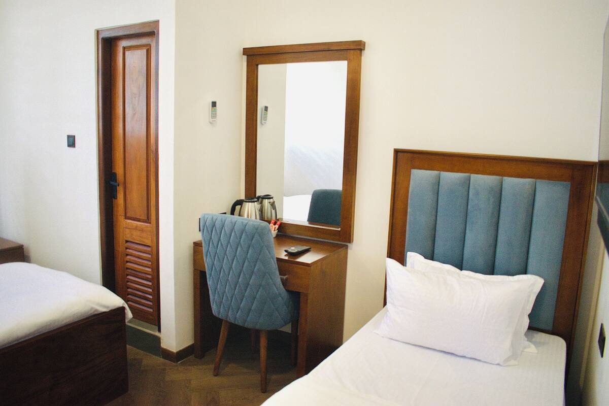 Quarto de hotel com cama, escrivaninha, cadeira, espelho e porta.