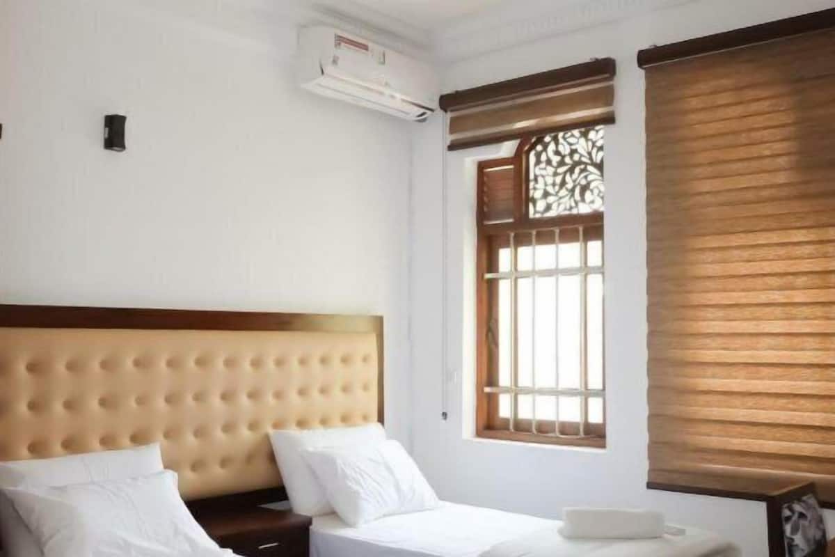 Quarto com cabeceira estofada, janela com grades e ar condicionado fixado na parede.