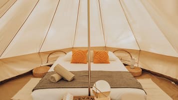 Acomodação em tenda com cama central, travesseiros, uma pequena mesa e um tapete tecido.