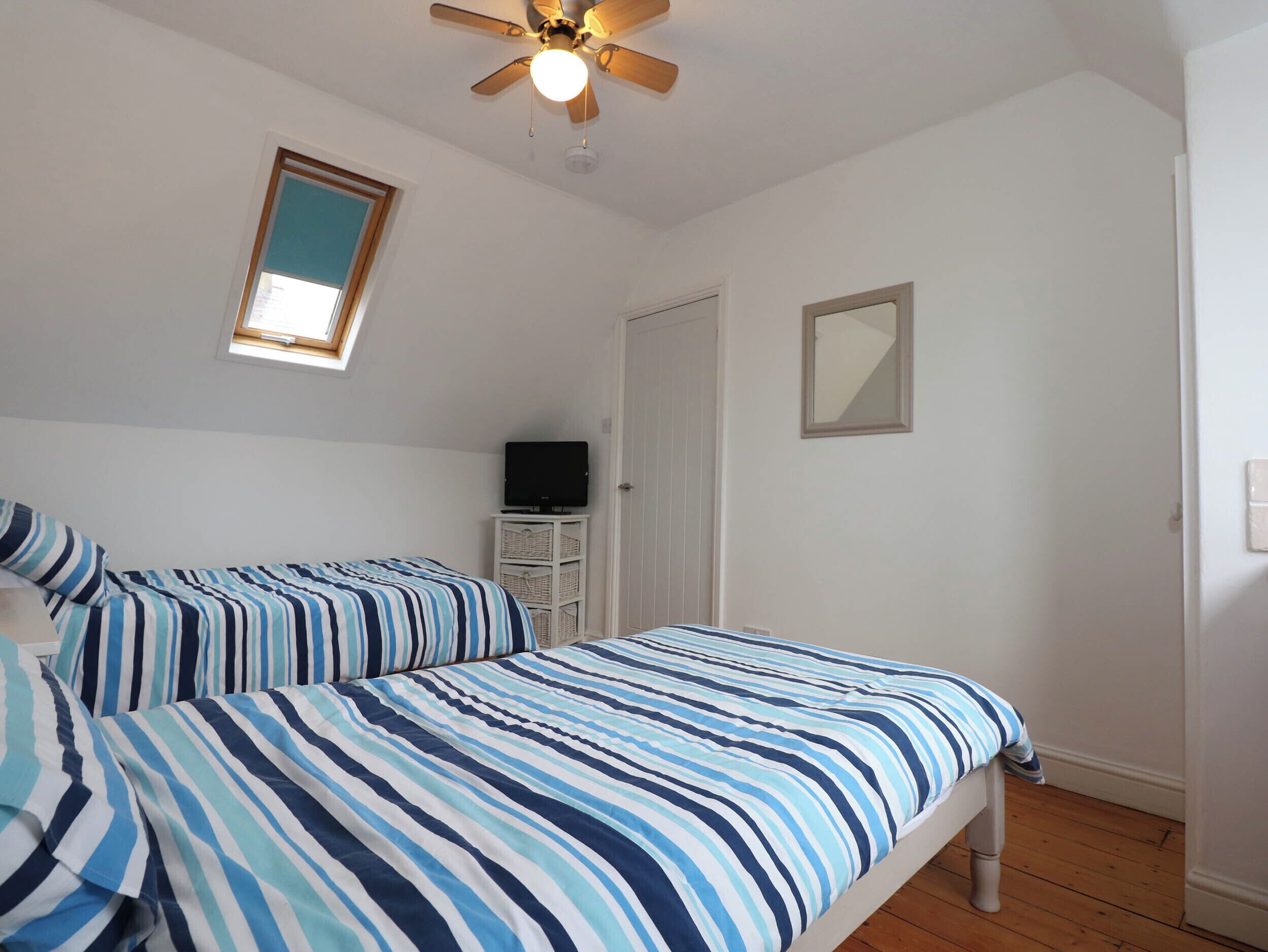 Quarto com duas camas, um ventilador de teto, uma TV sobre um armário branco e uma janela com vista.