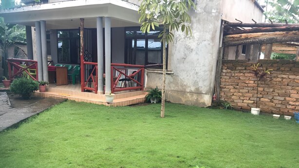 Uma casa com varanda coberta, parede de tijolos e pequeno jardim com grama e plantas em vasos.