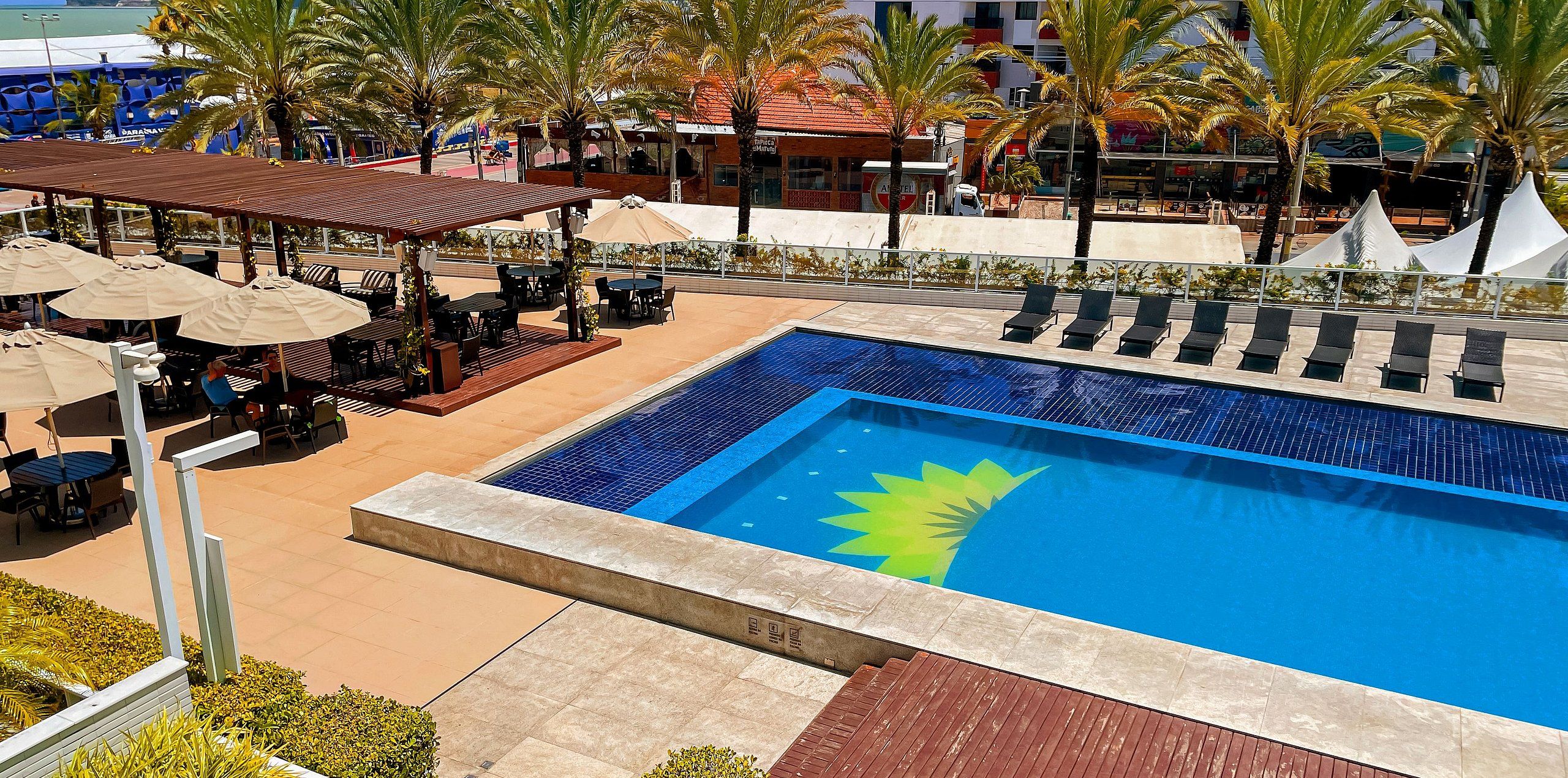 Área de piscina com um elemento aquático azul, cercada por espreguiçadeiras e guarda-sóis.
