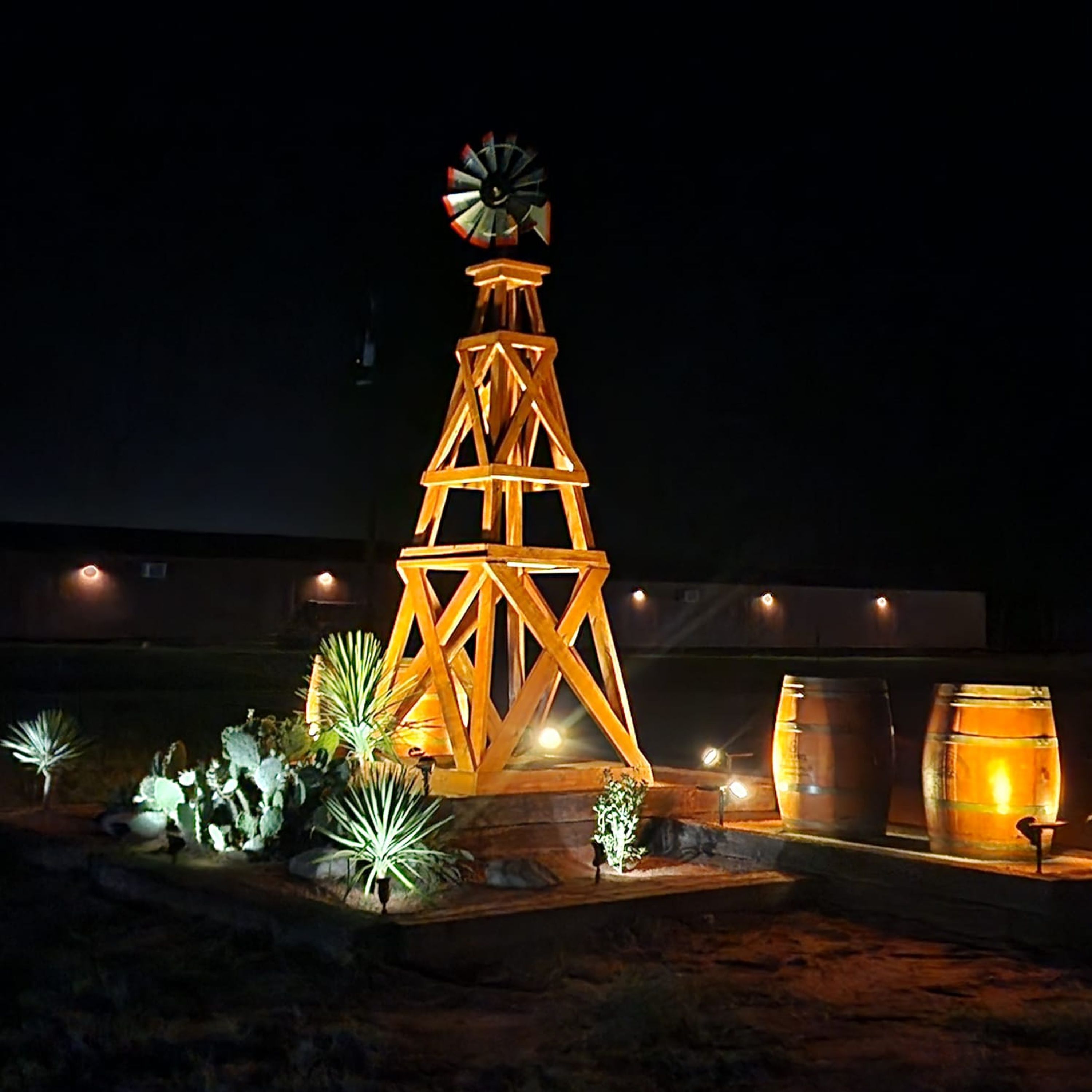 Uma estrutura em forma de pirâmide com um moinho de vento no topo, rodeada por plantas e iluminada por uma luz quente.