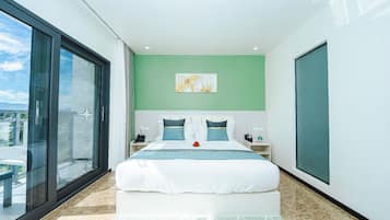 Quarto de hotel moderno com uma cama grande, vista através de uma porta de vidro deslizante, parede verde e um quadro sobre a cama.
