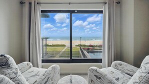 Quarto com uma grande janela com vista para uma praia, com piscina e espreguiçadeiras.