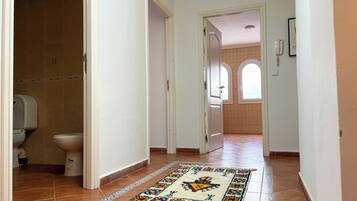 Um corredor com tapete estampado, soalho em azulejos e uma porta que dá para um banheiro.