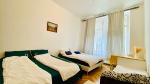 Quarto de hotel com duas camas, uma mesinha com um vaso e uma janela com cortinas.